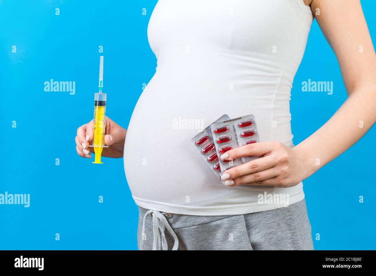 Close up of pregnant woman holding a syringe and blisters with pills. A ...