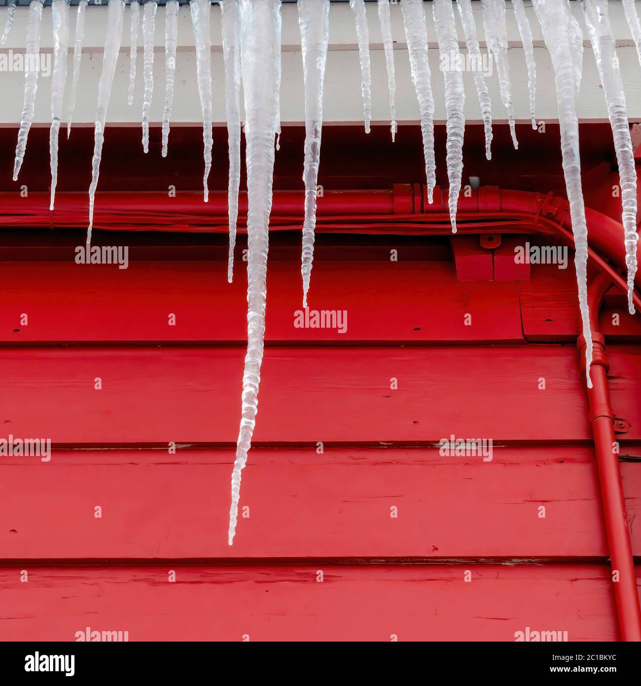 Square crop Spiked frozen icicles at the roof of home with vibrant red ...