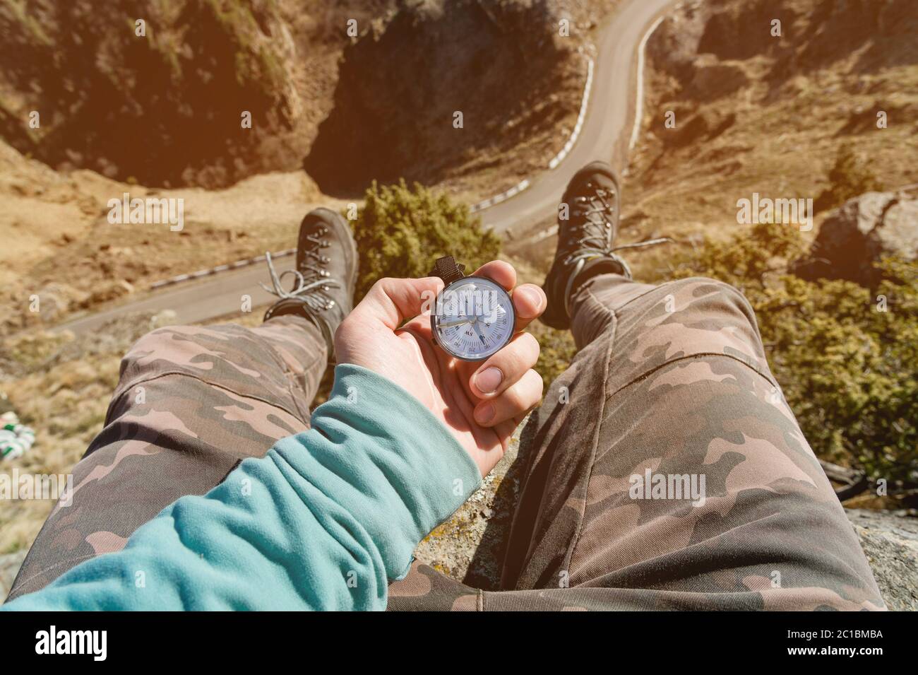 Hiker sitting on a high rock holds a compass in front of her feet in ...