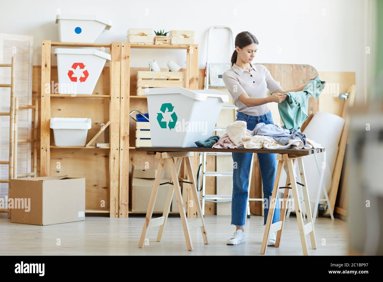 Young woman examining her old clothes and sorting them into the ...