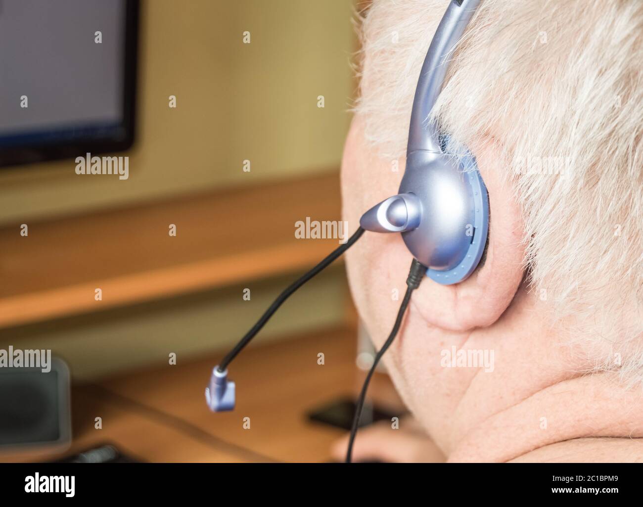 A gray-haired fat old man with a headset looks at the monitor screen ...