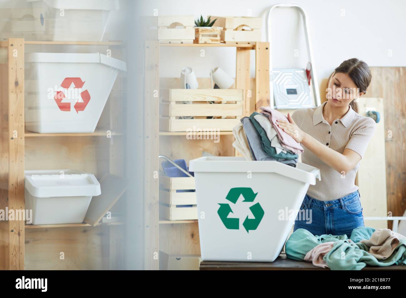 Young woman putting her old clothes into eco plastic bin she recycling ...