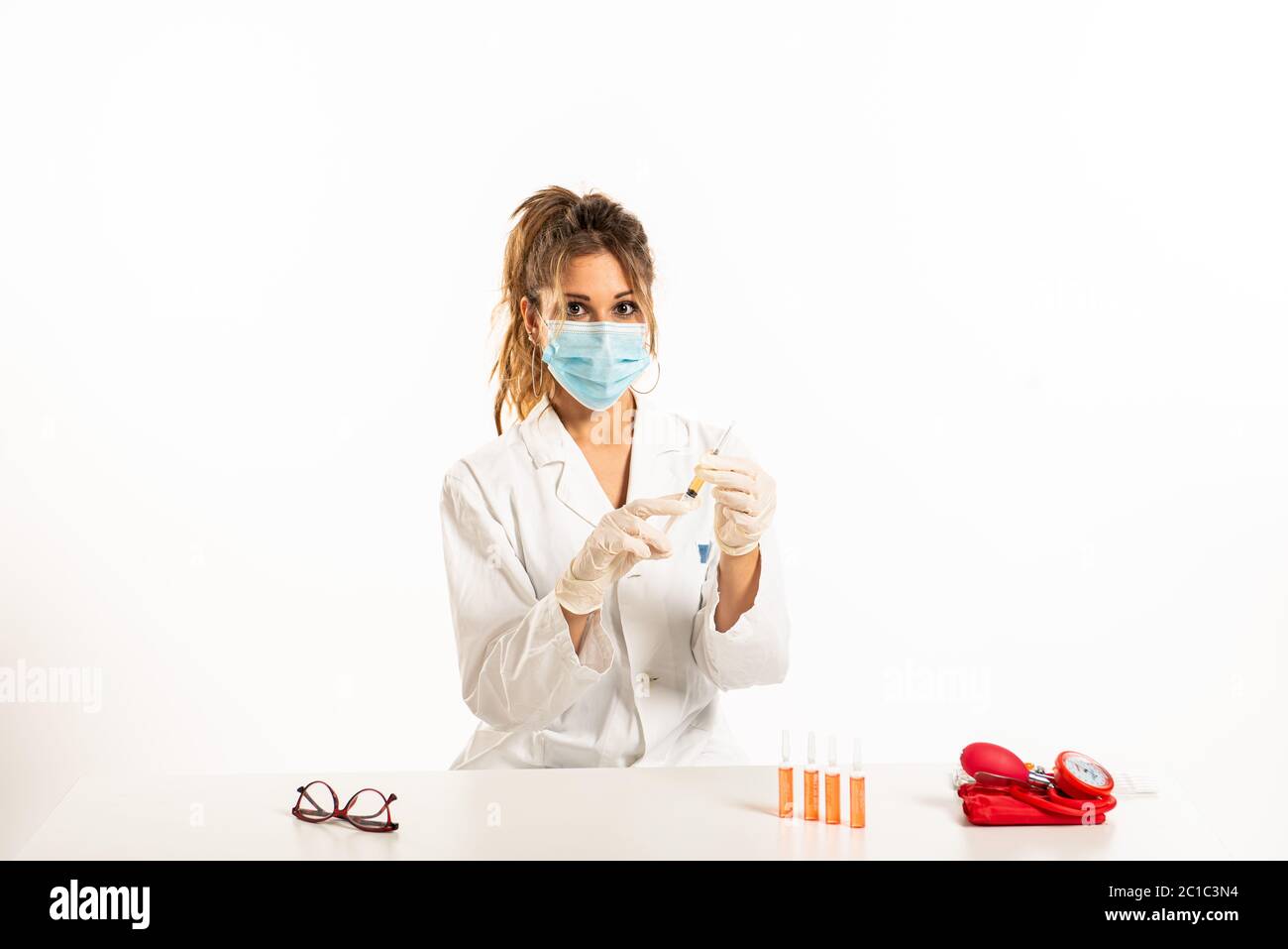 Woman wearing medical uniform preparing syringe behind table with other ...