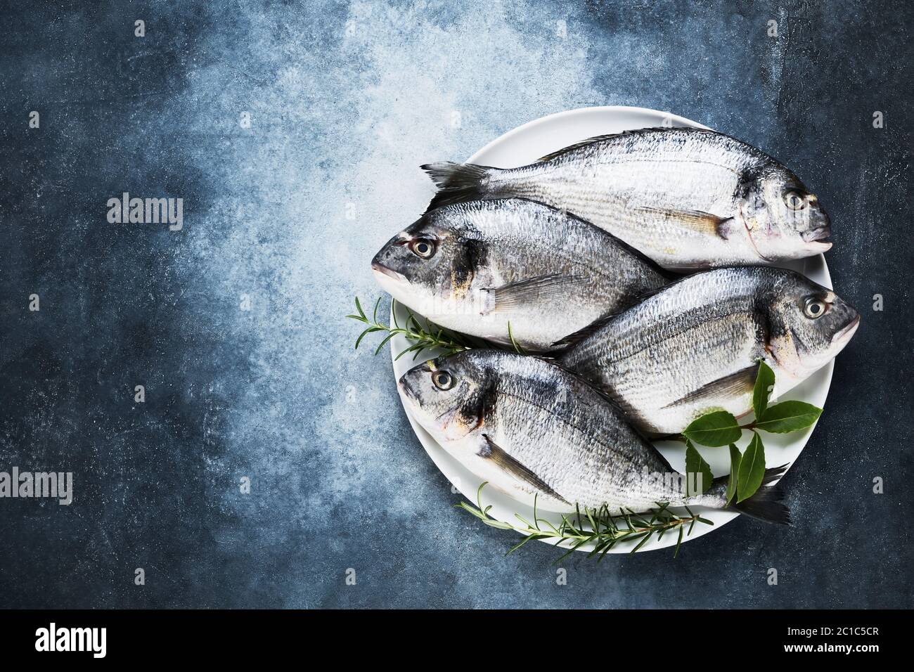 Four Fresh Royal Dorado fish on a white dish on blue backdrop. Healthy ...