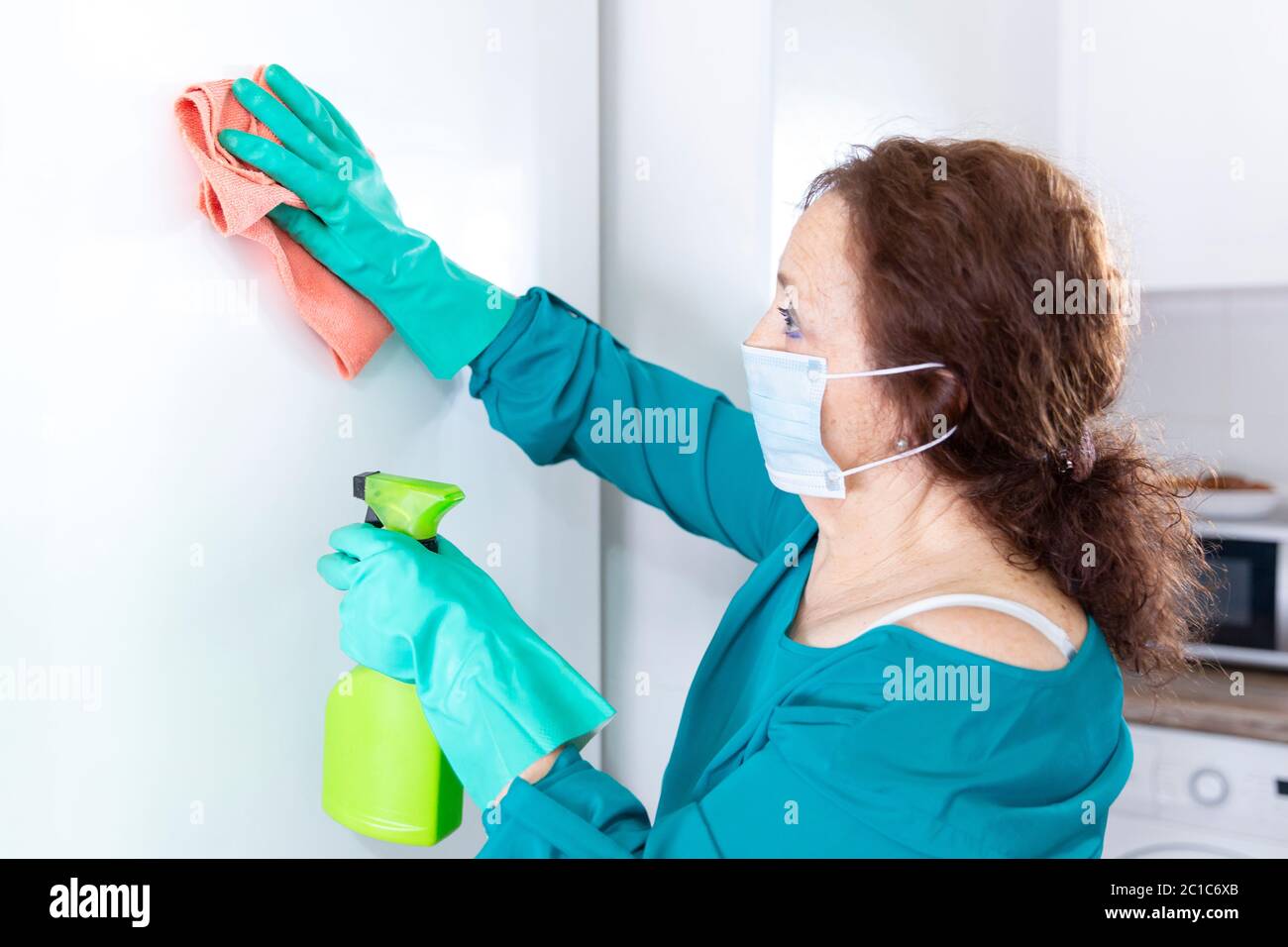Woman disinfecting surfaces in her home with gloves and protective face ...