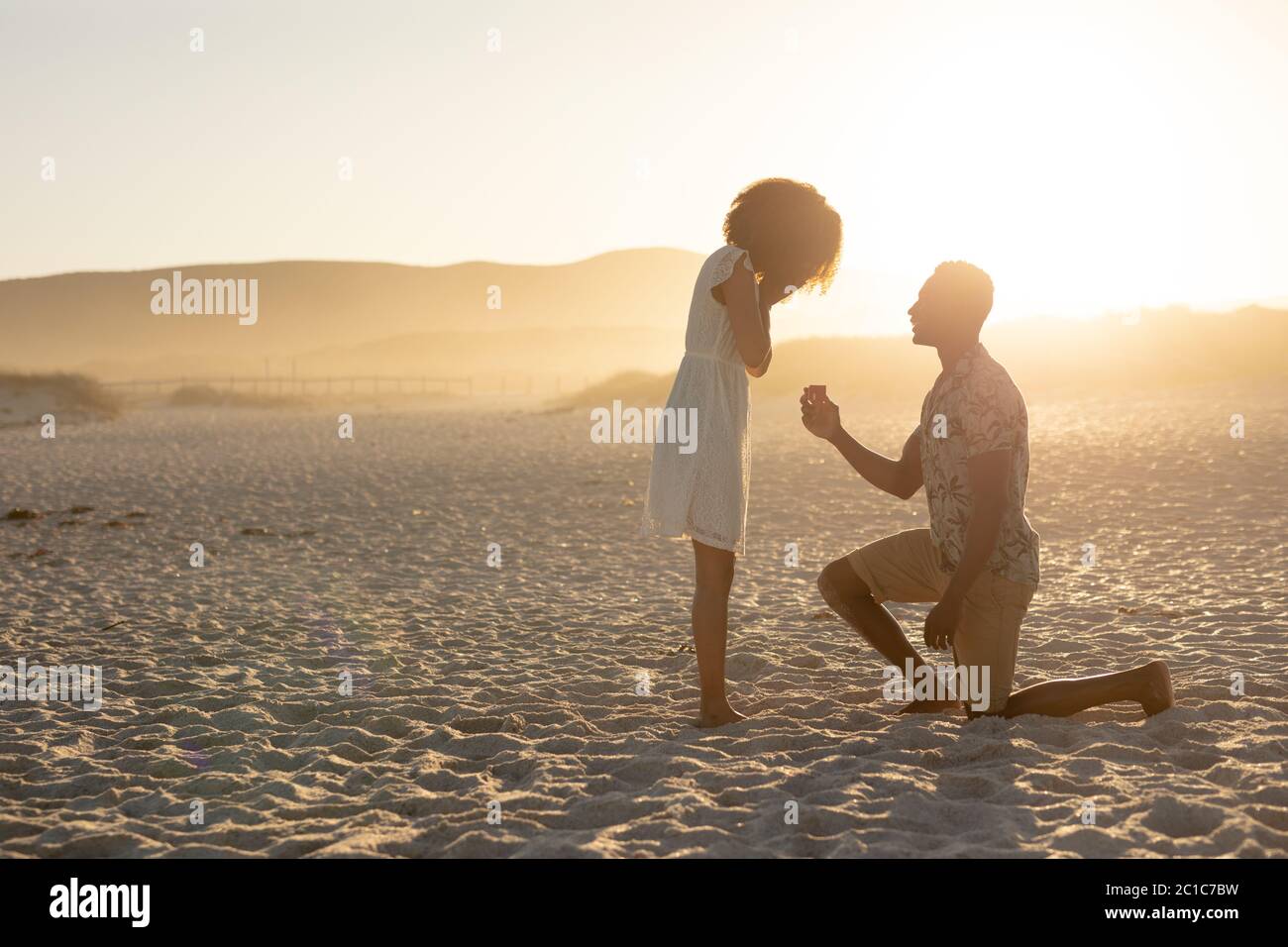 An African American man proposing to the woman on beach on a sunny day ...