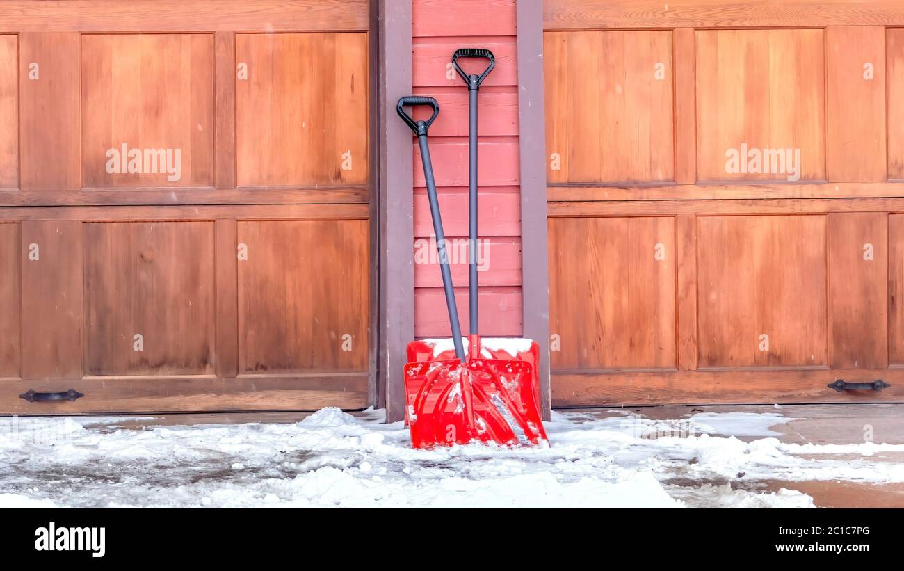 Panorama Red shovels on snowy driveway against wall and wooden garage ...
