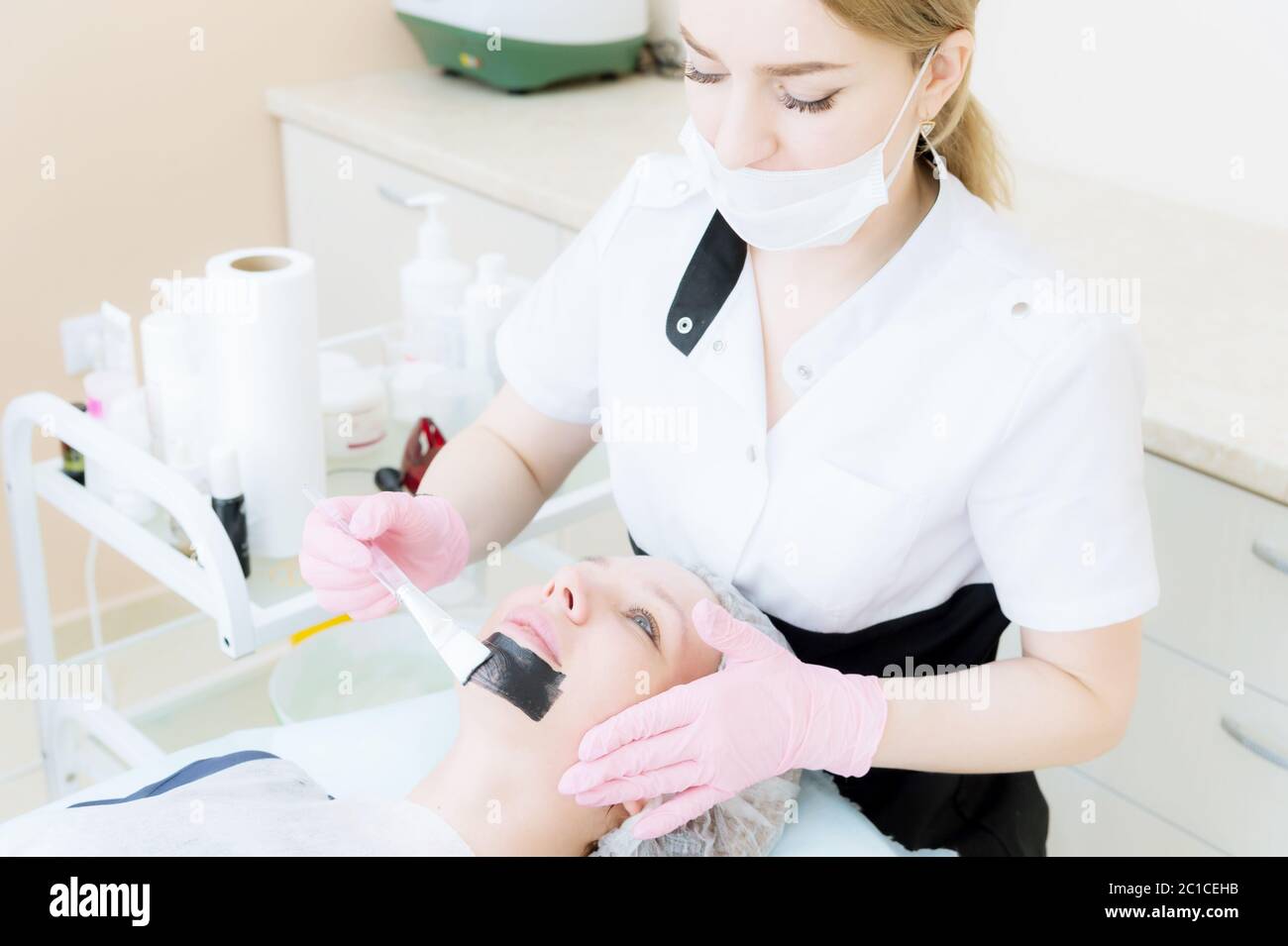The Cosmetologist In Pink Gloves With A Brush Applies A Carbon Mask For