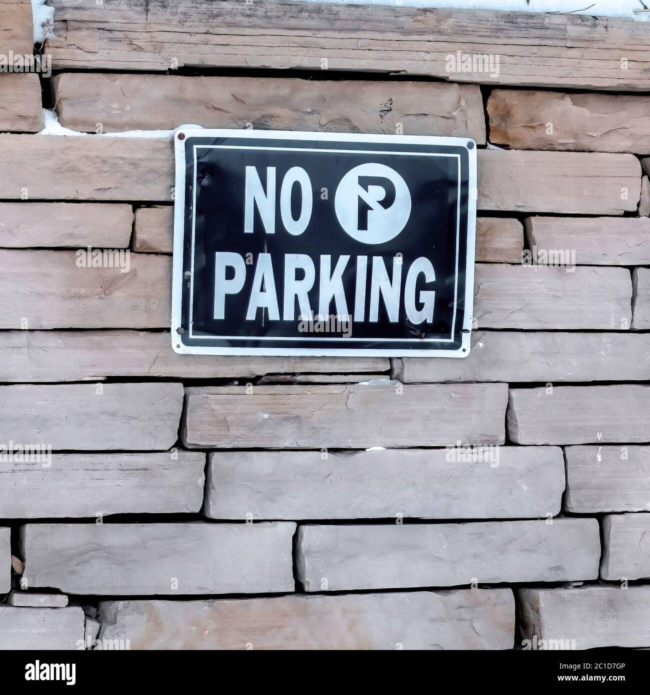 Square No Parking sign on a stone brick retaining wall topped with snow ...