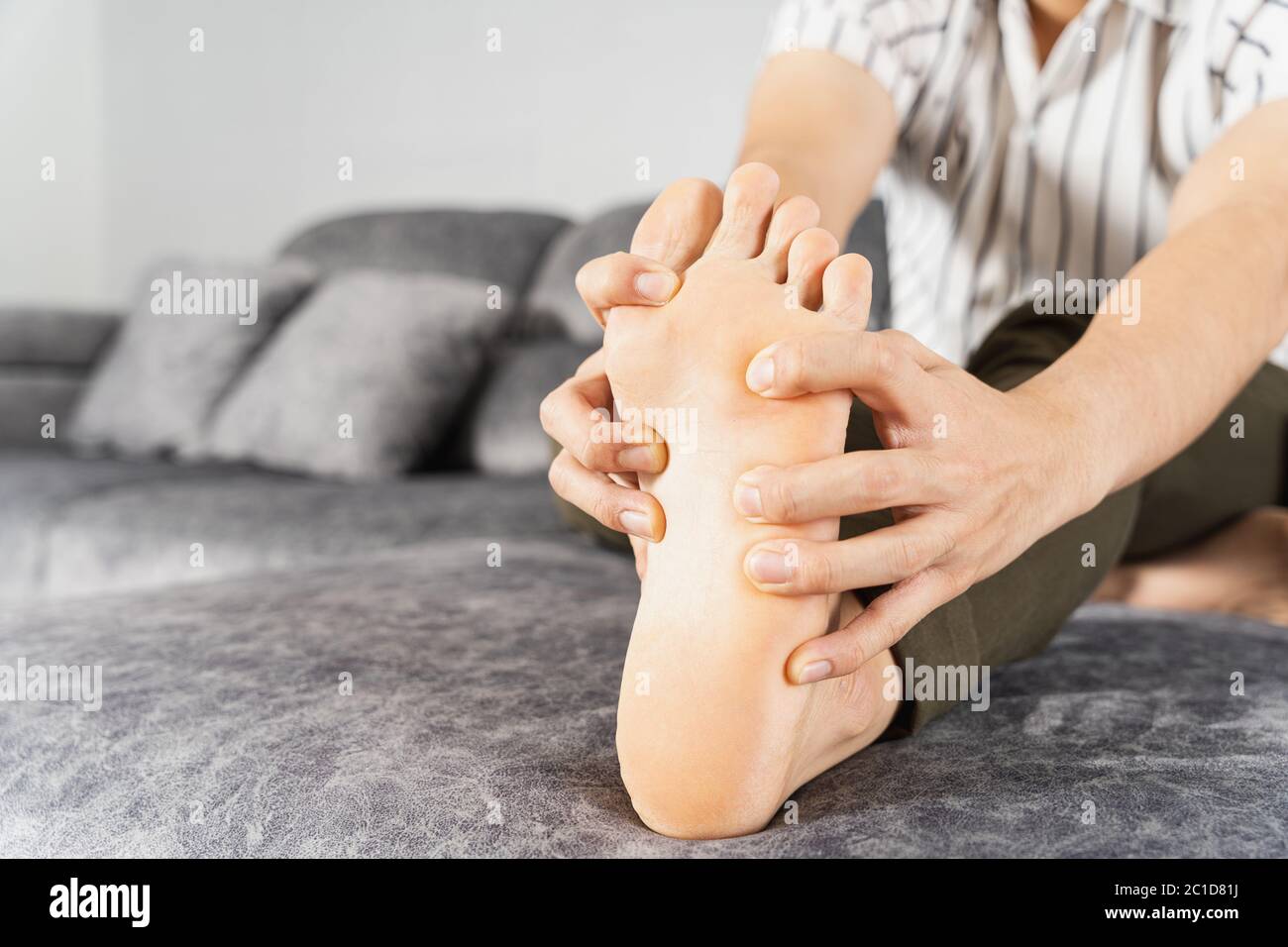 Young man suffering from foot pain while sitting on sofa at home ...