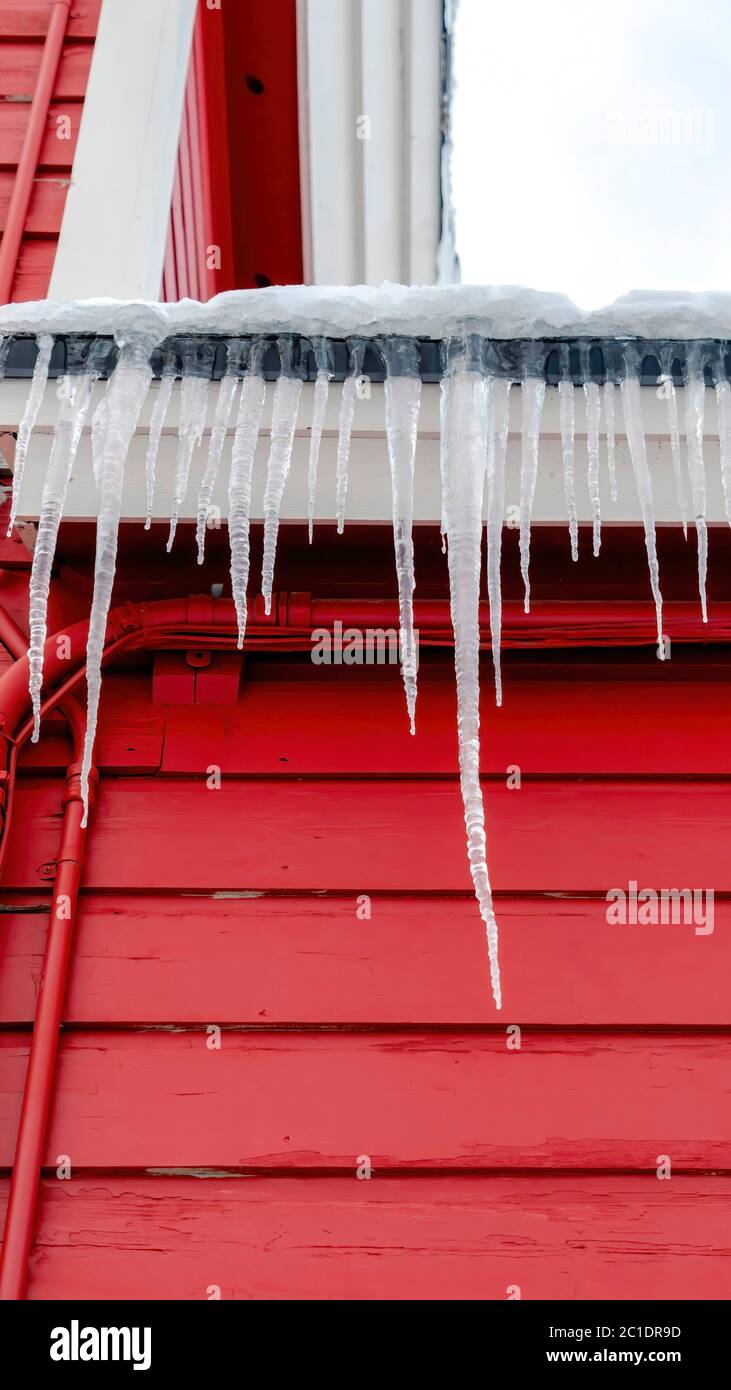 Vertical frame Spiked frozen icicles at the roof of home with vibrant ...