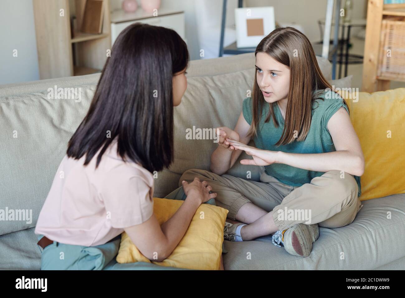 Teenage girl sitting with crossed legs on sofa and gesturing hands ...