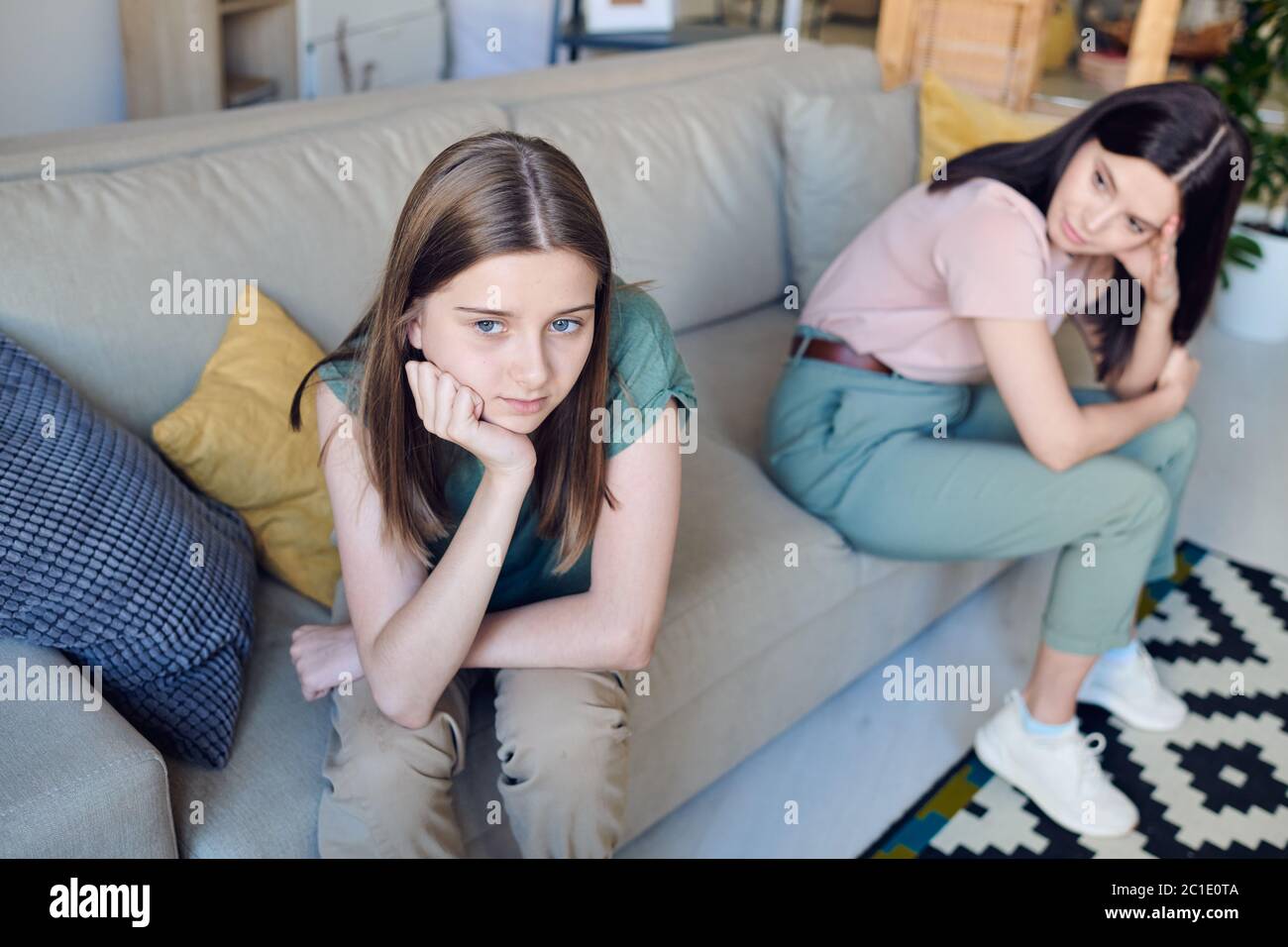 Sad teenage girl being in conflict with mother sitting on sofa and ...