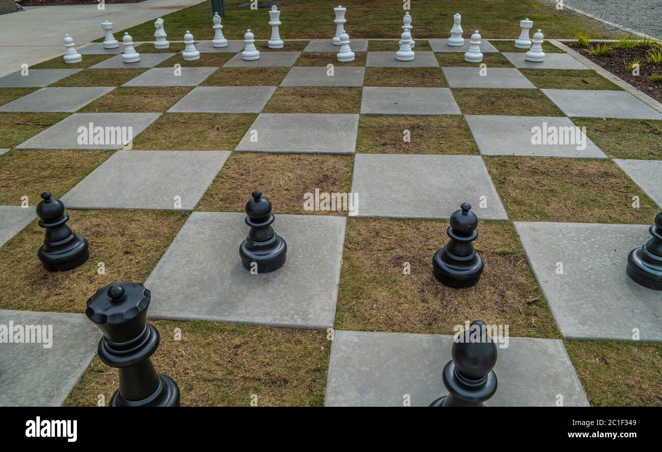 Looking downward at a giant outdoor chess set on cement and grass ...