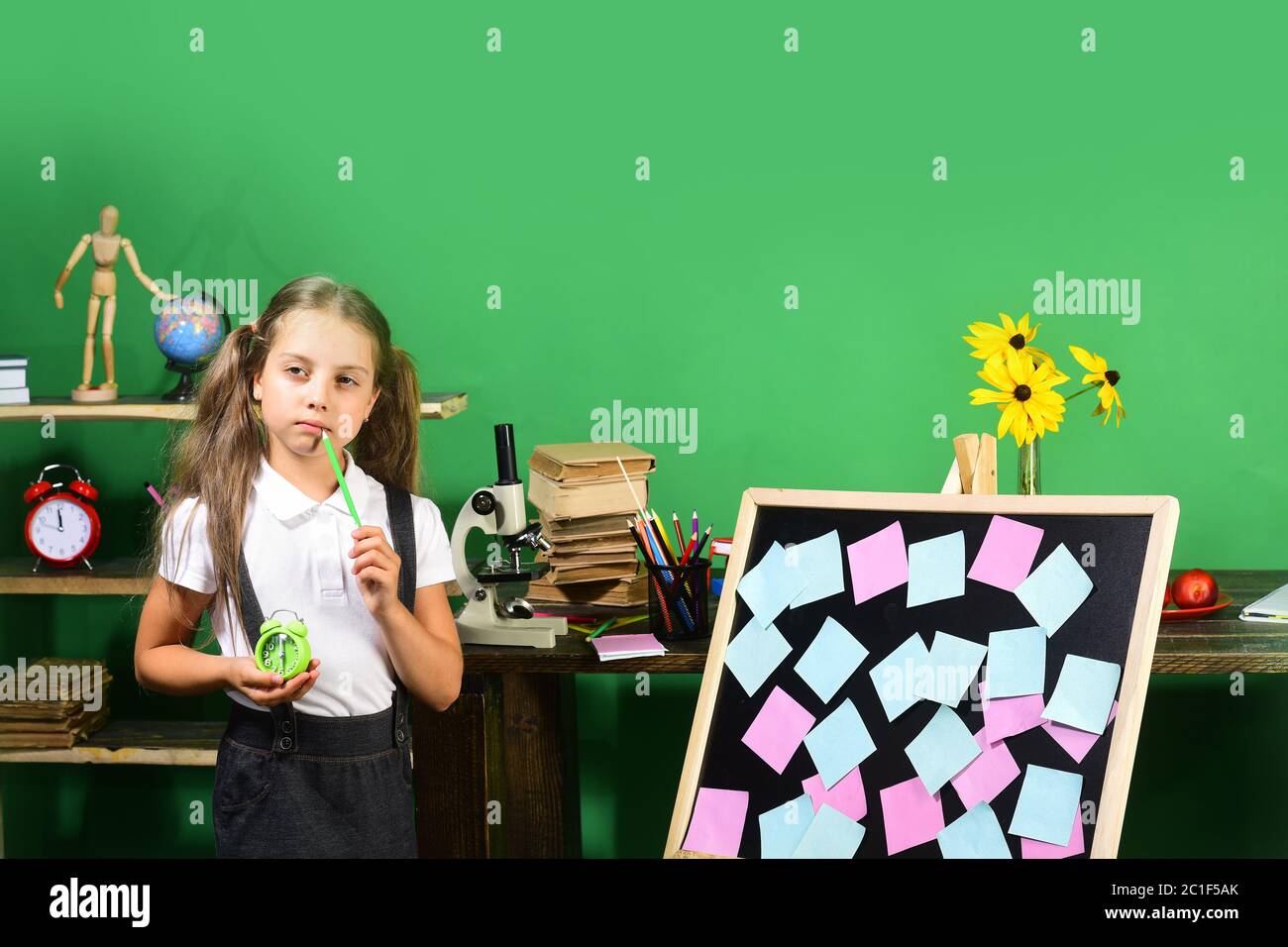 Childhood and study time concept. Girl holds green clock and pencil by ...