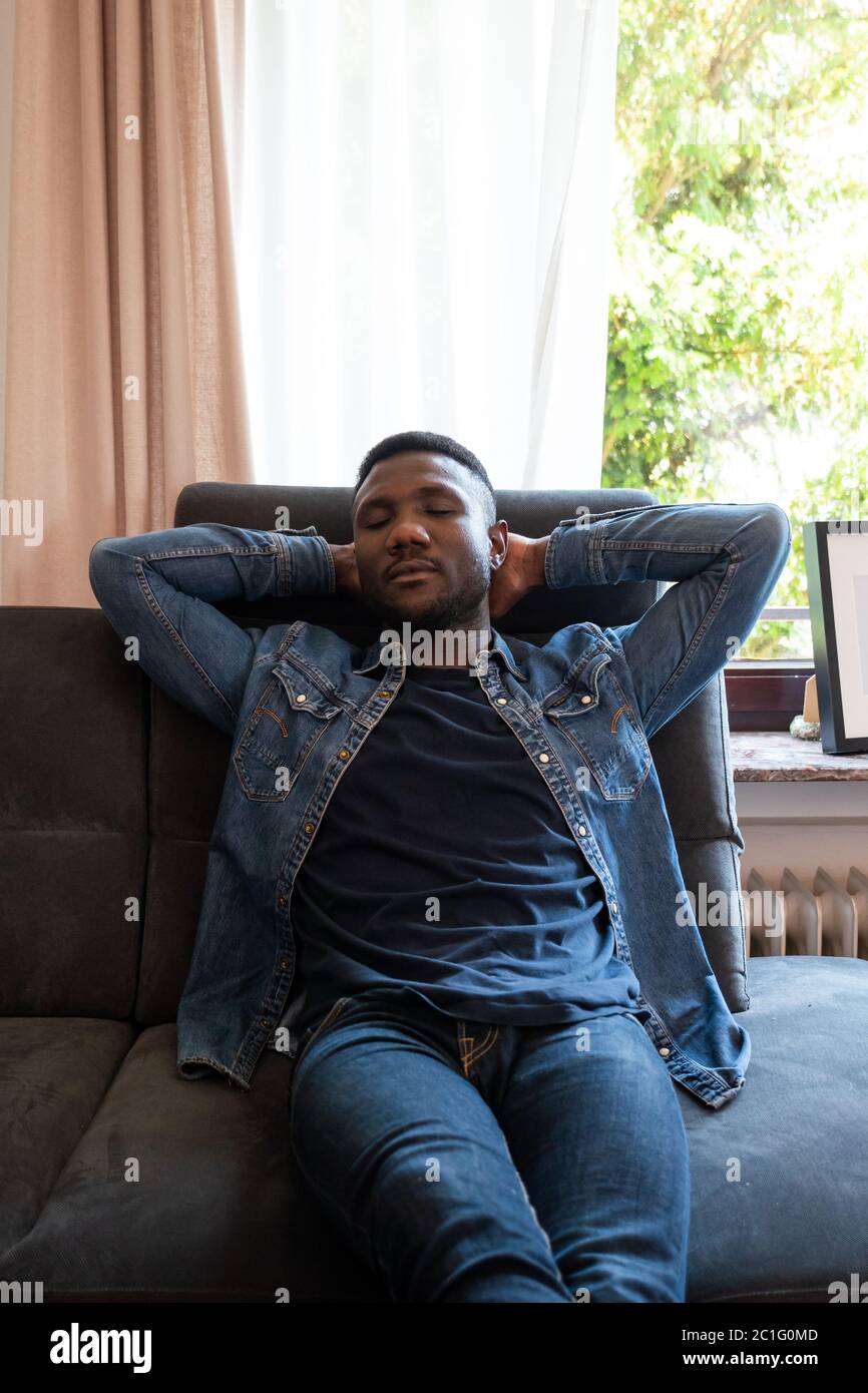 Young Black man napping on living room sofa with hands behind head ...