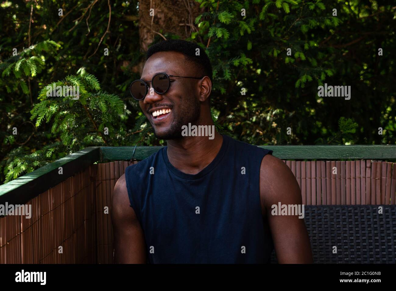 Young black man in sunglasses seated looking away smiling. Medium shot ...