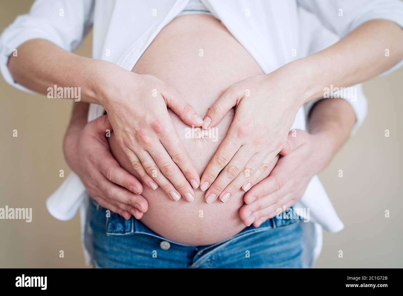 Pregnant woman with her husband hugging tummy, heart symbol on belly ...