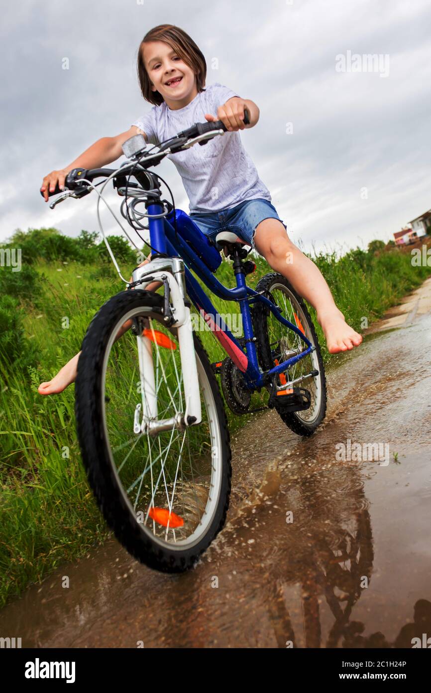 Child, boy, riding bike in muddy puddle, summer time on a rainy day ...