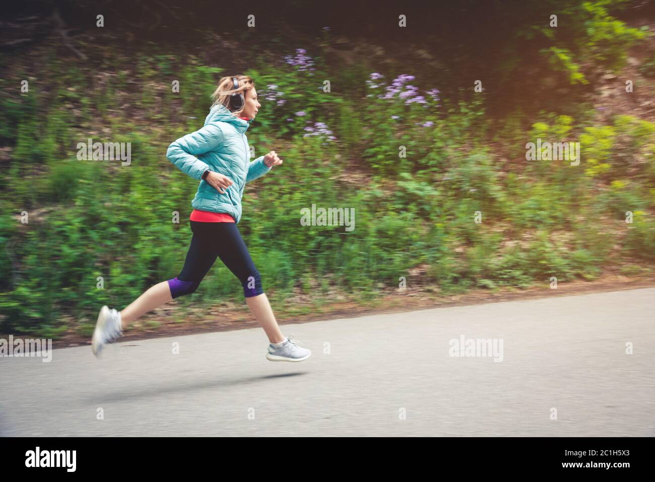 A young blonde woman running is practicing outdoors in a city mountain ...