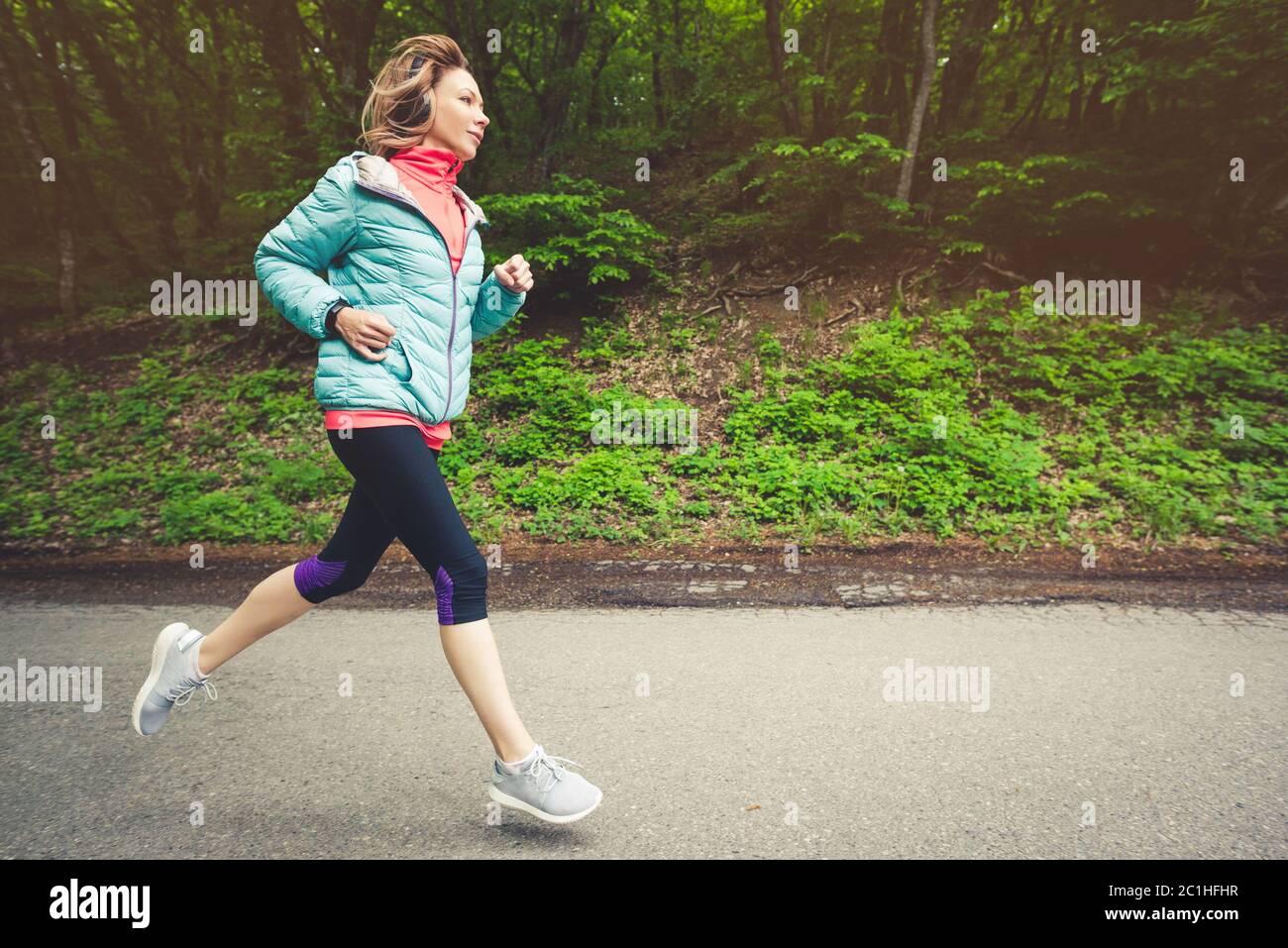 A young blonde woman running is practicing outdoors in a city mountain ...