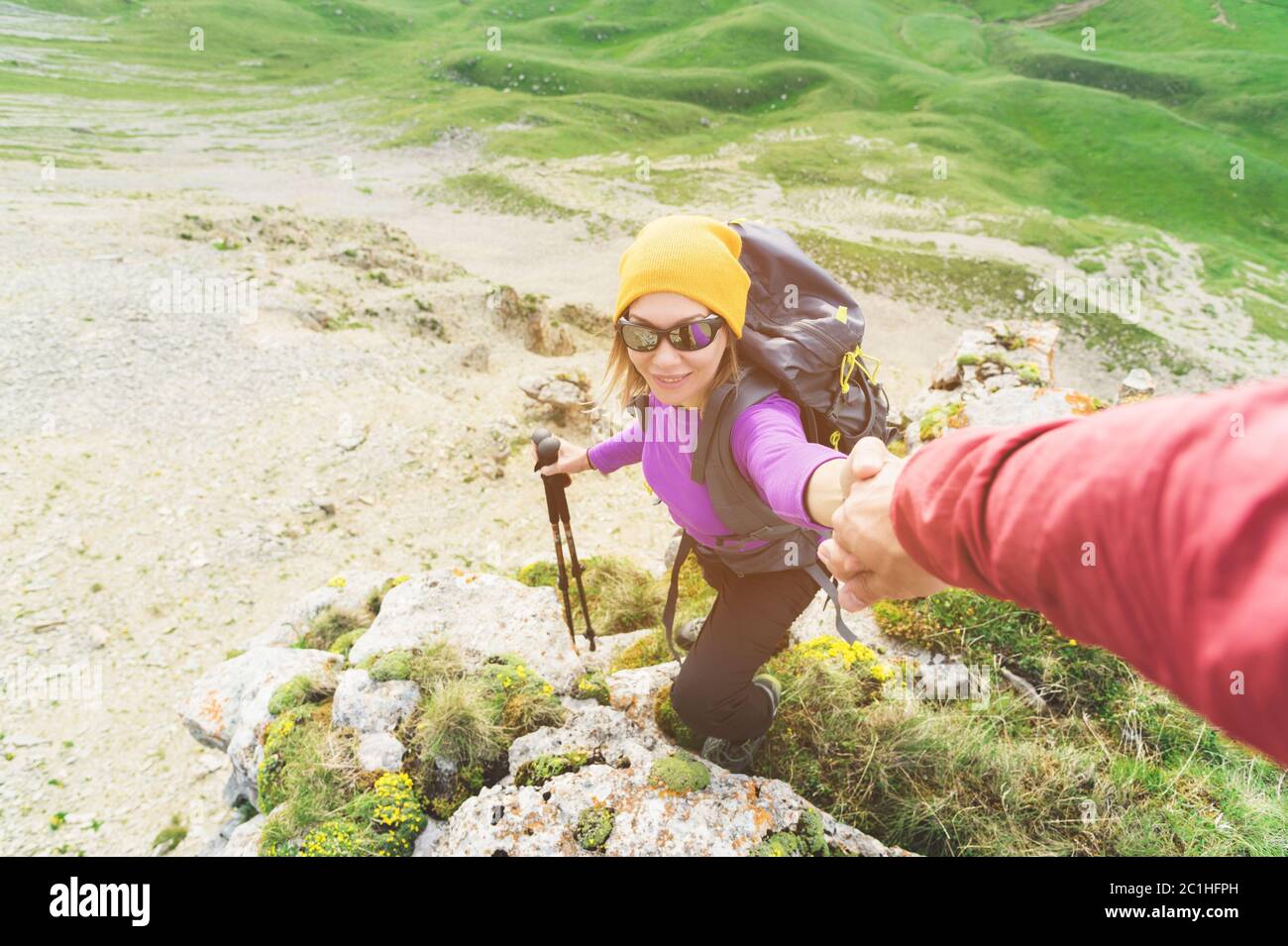 A climber helps a young mountaineer woman reach the top of the mountain ...
