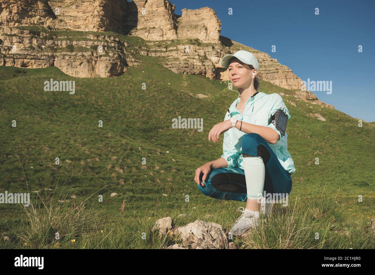 Athlete cute girl in cap with headphones getting ready to run on nature ...