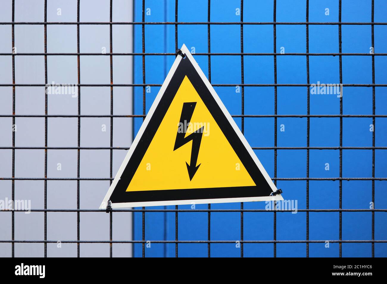 High voltage triangle warning sign mounted on a metal lattice fence on ...