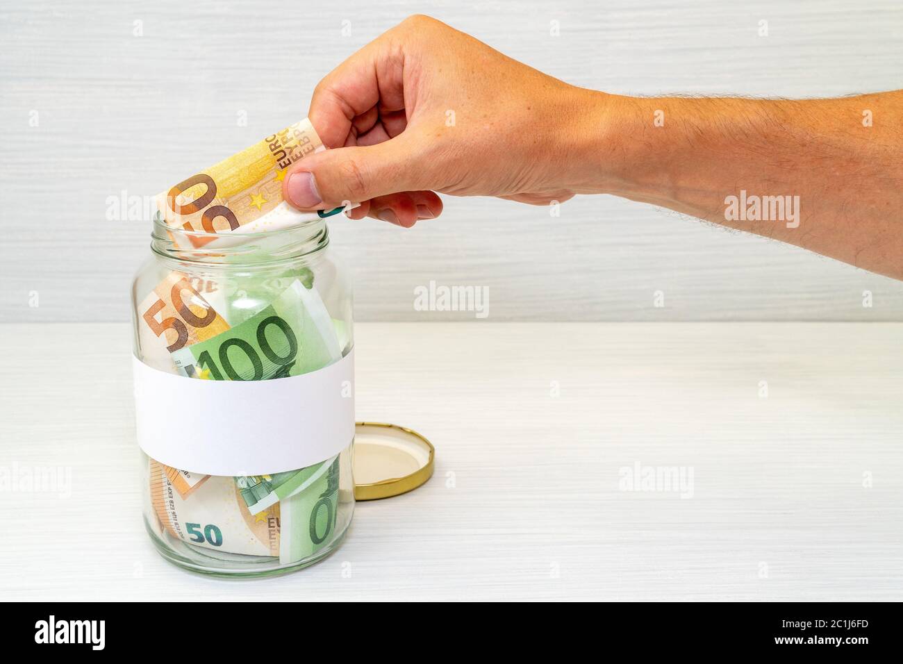 Hand puts money in jar Stock Photo - Alamy