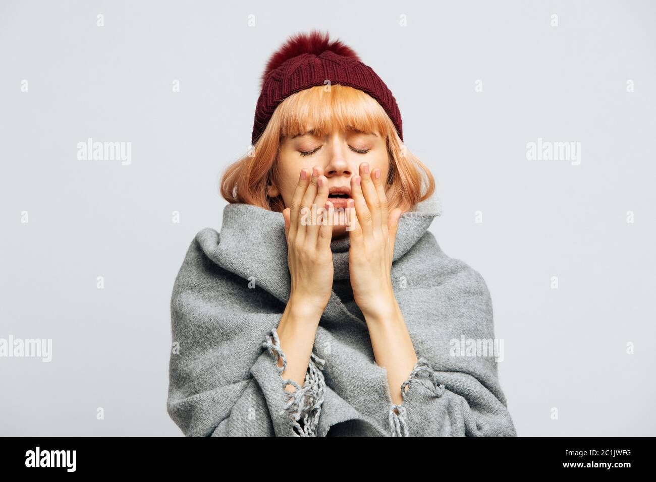 Cute unhealthy female in red hat, wrapped in warm scarf sneezing ...