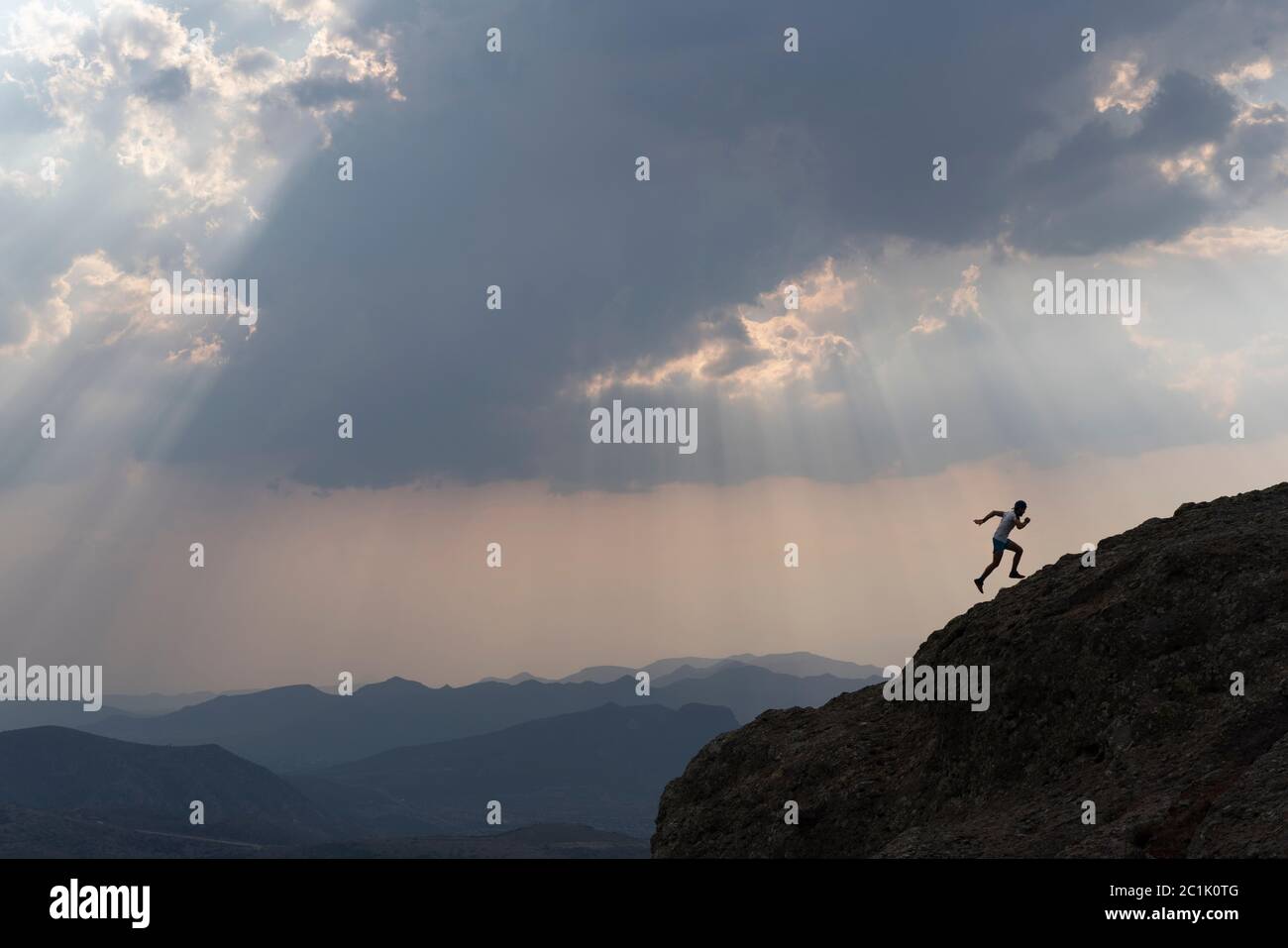 One man running up on a rock under a cloudy sky with sun rays Stock ...