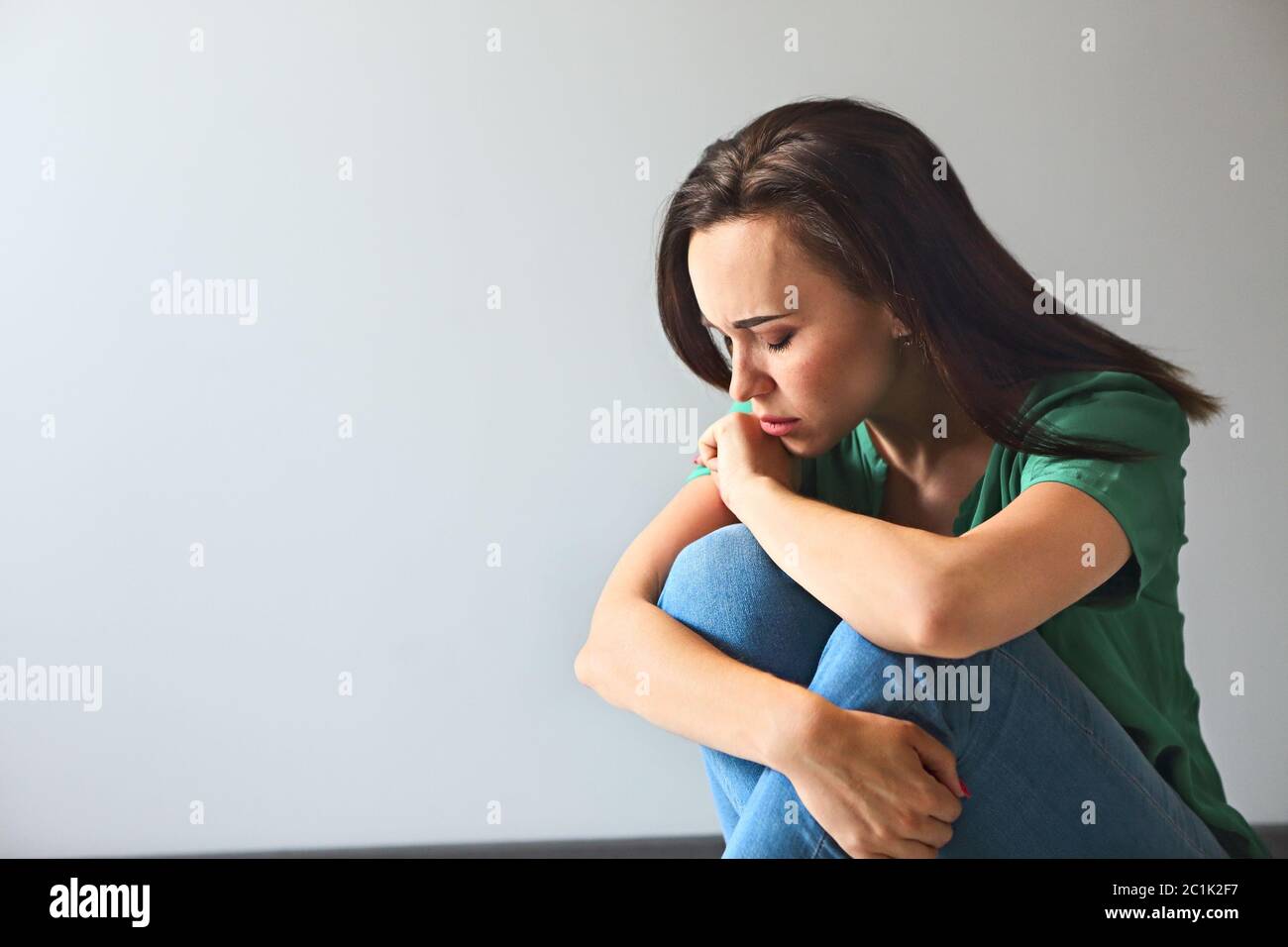 Sad woman looking thoughtful about her troubles in front of a gray wall ...