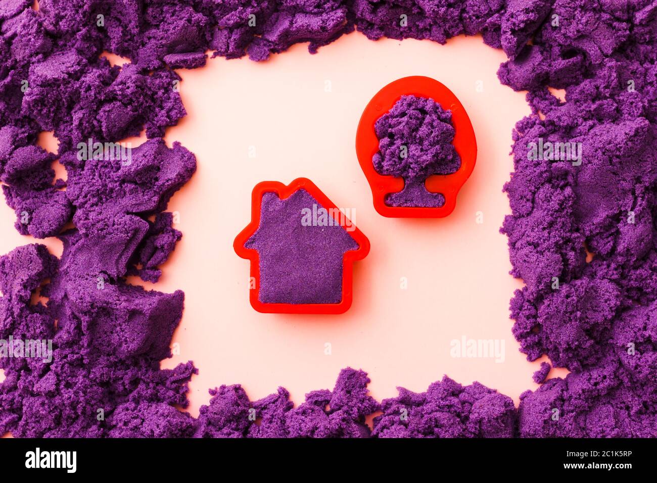 Violet kinetic sand in shape of house and tree in a red frame ...