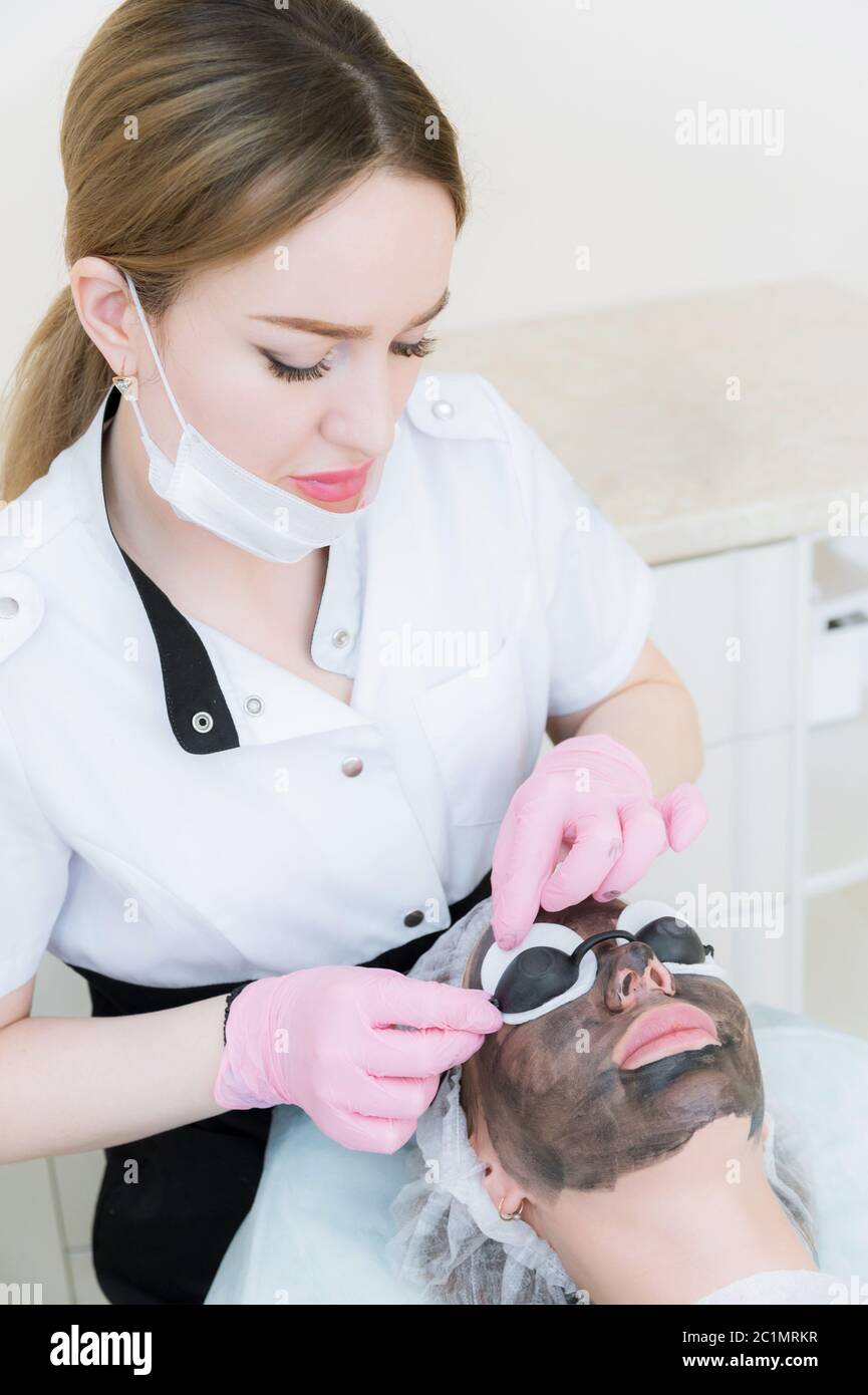The Cosmetologist In Pink Gloves With A Brush Applies A Carbon Mask For