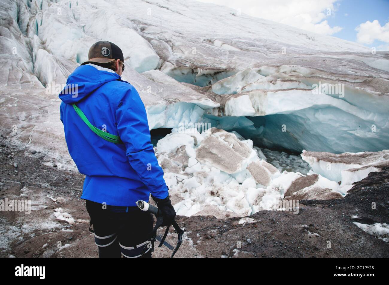 A young guide in a cap with climbing equipment and an ice ax in his ...