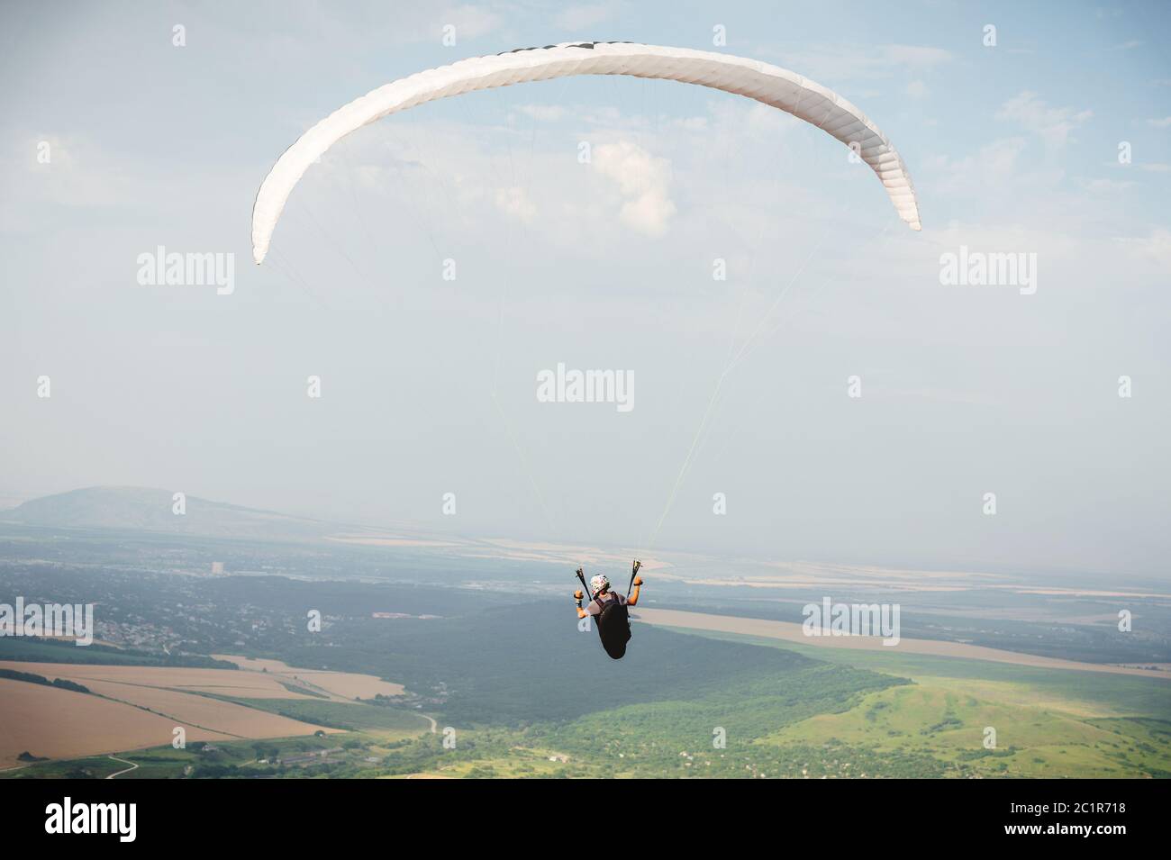 Professional paraglider in a cocoon suit flies high above the ground ...