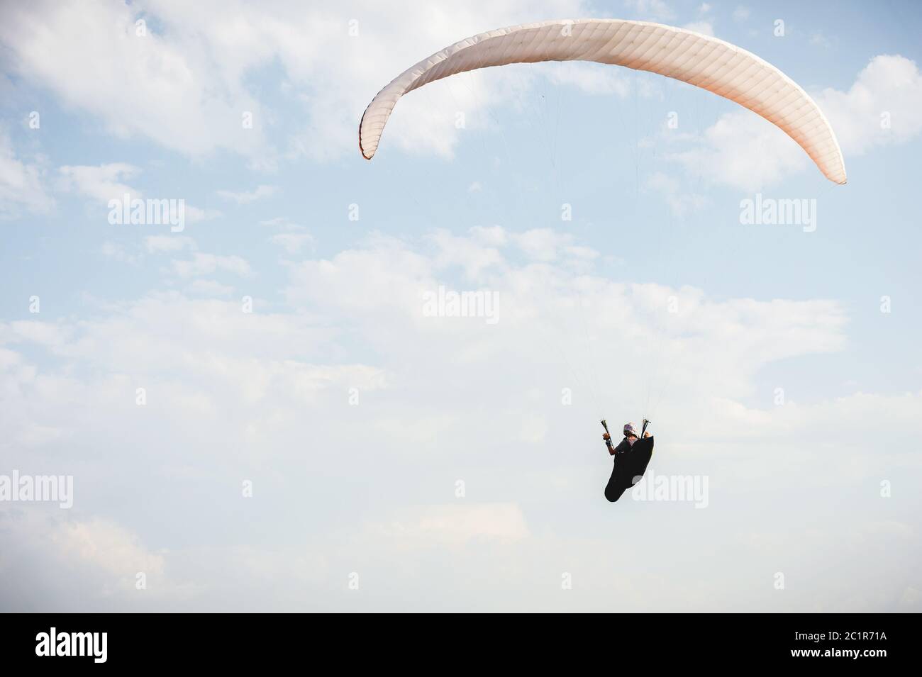 Professional paraglider in a cocoon suit flies high above the ground ...