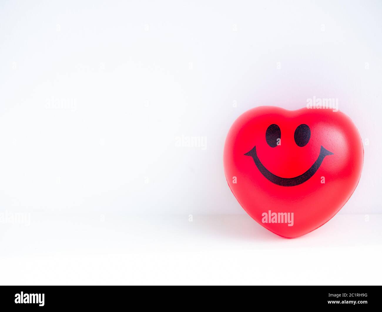 Red heart. Happy smiley face on big red heart ball on white clean table ...