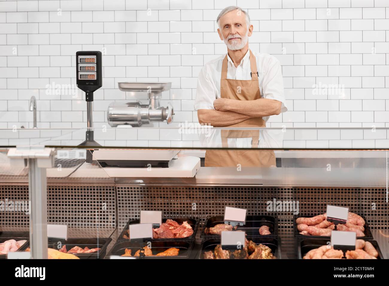 Portrait of senior male butcher with crossed arms posing in apron ...