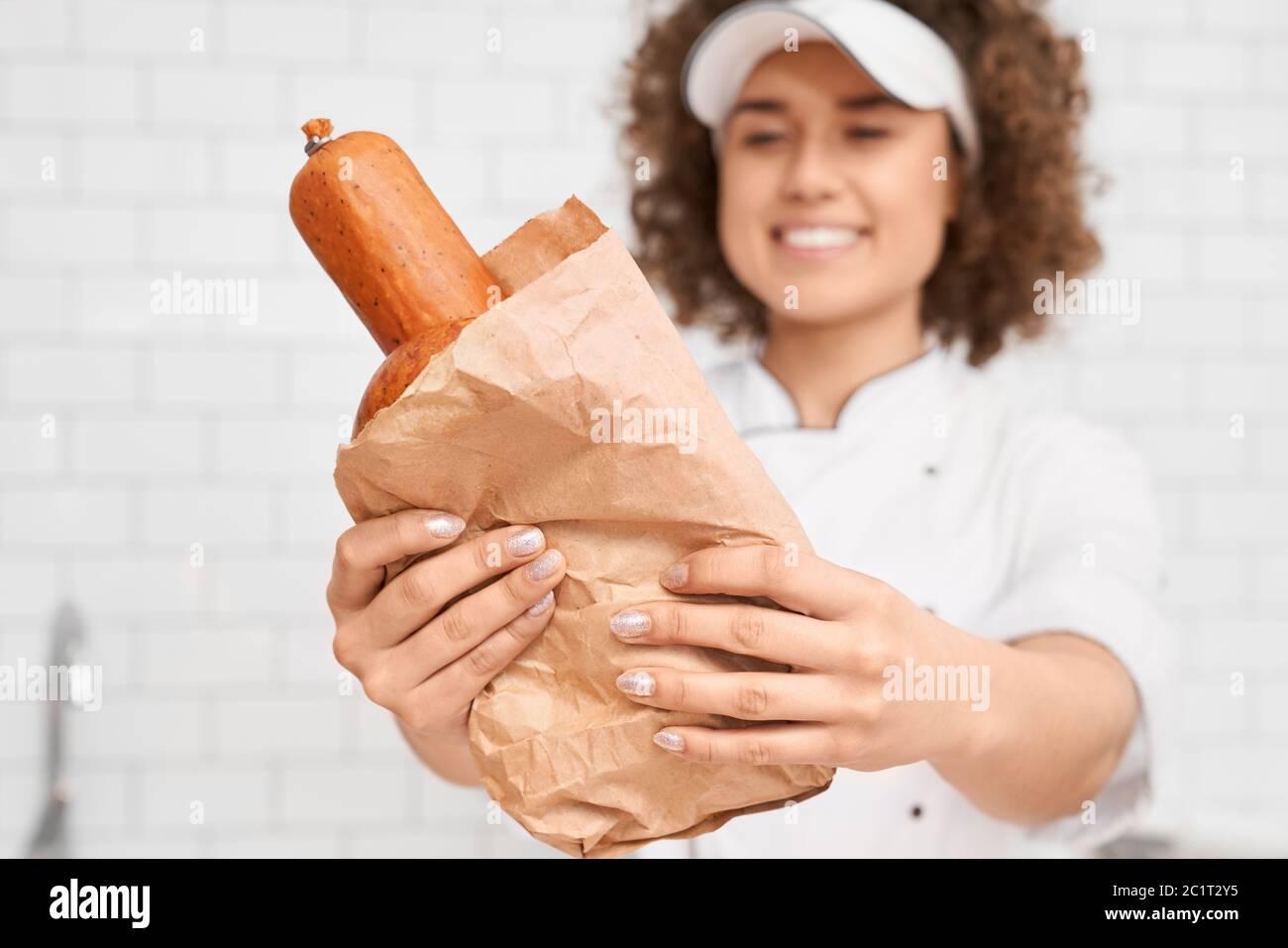 Crop of young smiling woman with curly hair giving meat products ...