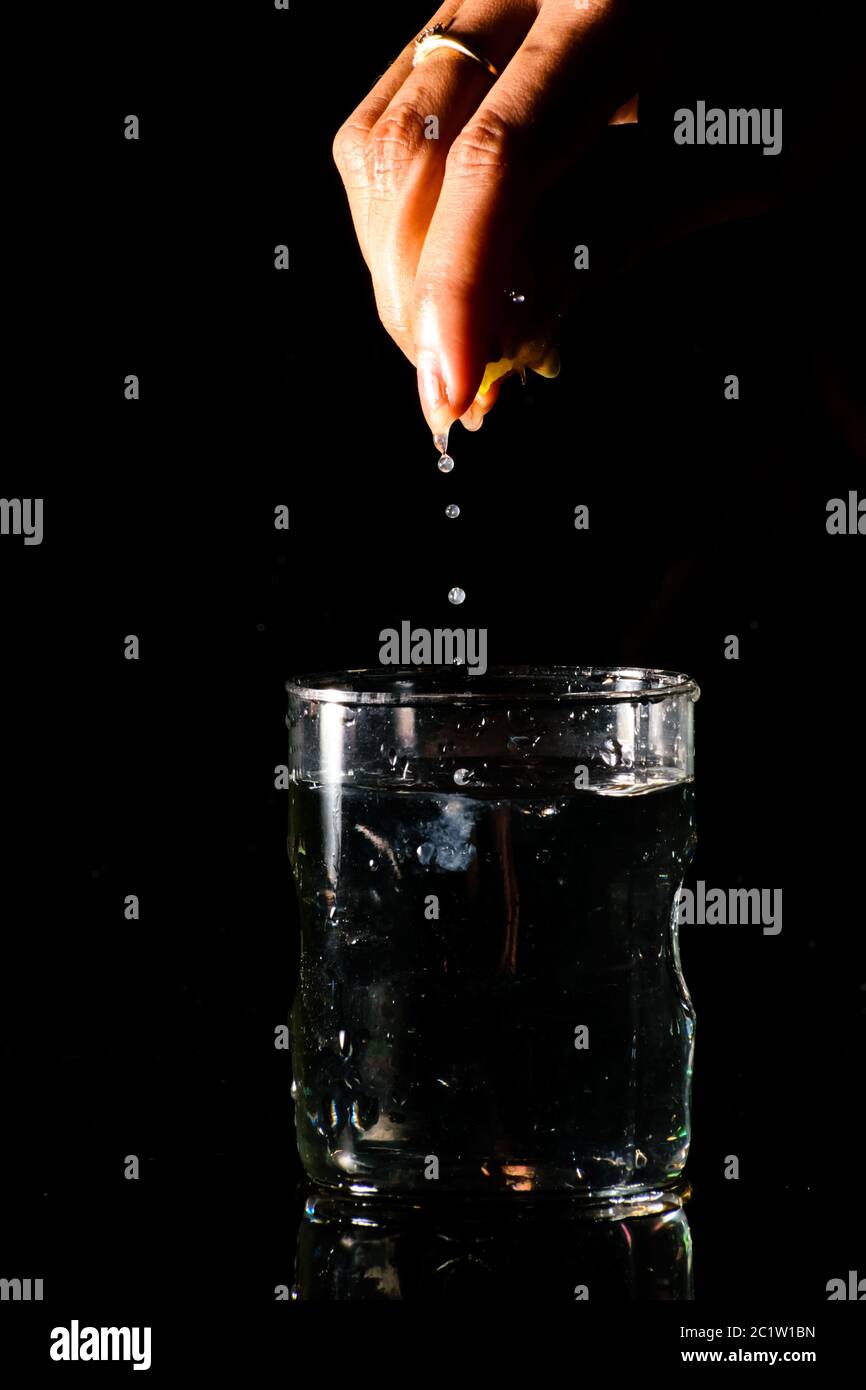 A Glass Of Water Placed On A Reflective Surface In A Dark Background And A Piece Of Cut Lemon Is a-glass-of-water-placed-on-a-reflective-surface-in-a-dark-background-and-a-piece-of-cut-lemon-is