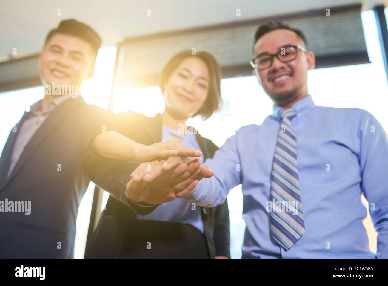 Group of three Asian business people joining their hands making unity gesture symbolizing ...