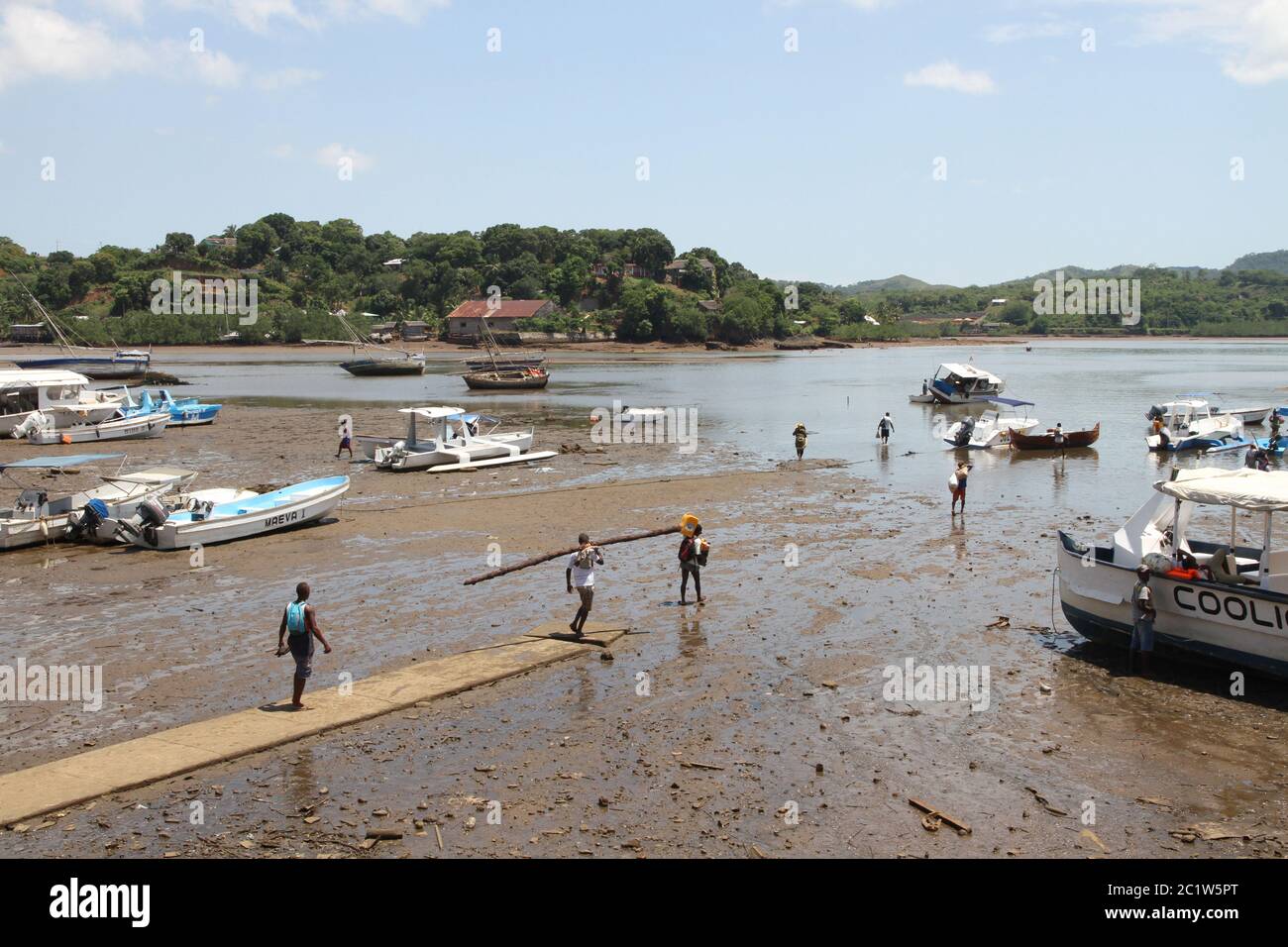 Beached boats and man carrying log in Andoany Harbour or Hell-Ville ...