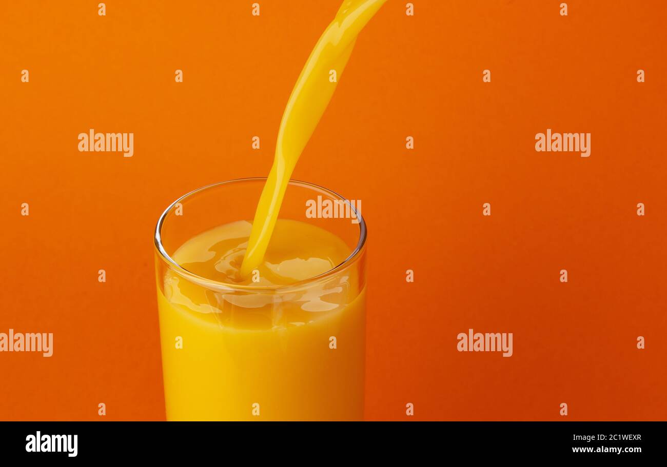 Orange juice pouring into glass, isolated on colour background, with ...