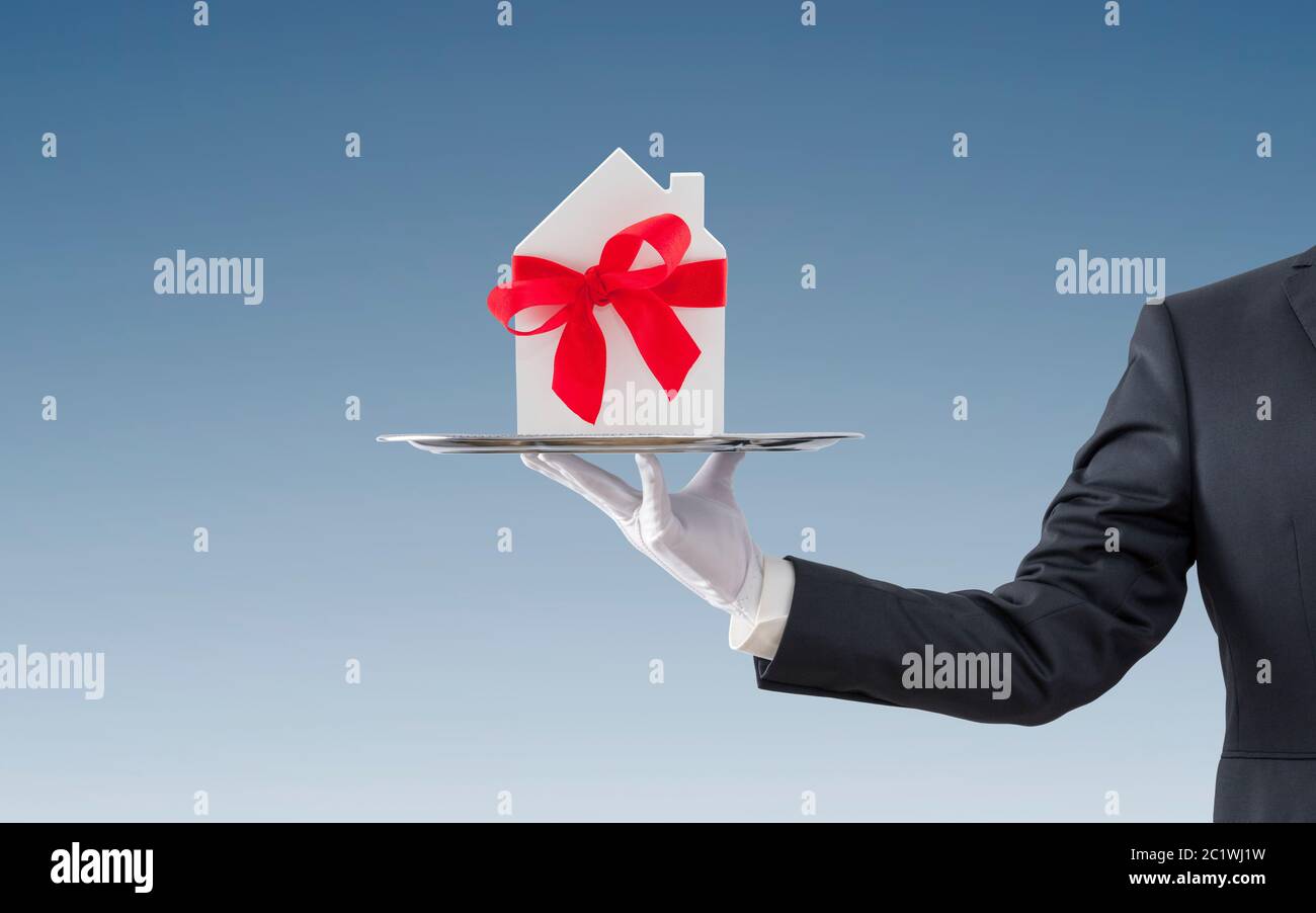 Businessman offering house with red ribbon on silver tray over blue ...