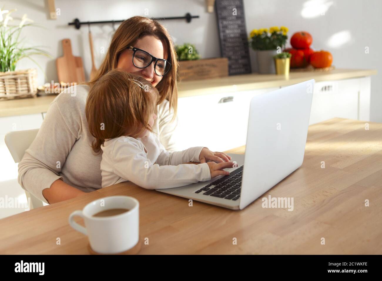 Smiling mom working at home on a laptop computer while taking care of ...