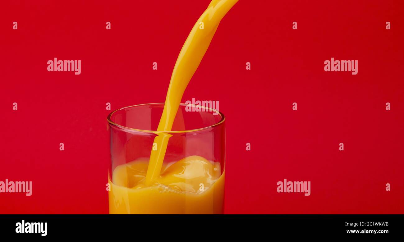 Orange juice pouring into glass, isolated on red color background, with ...