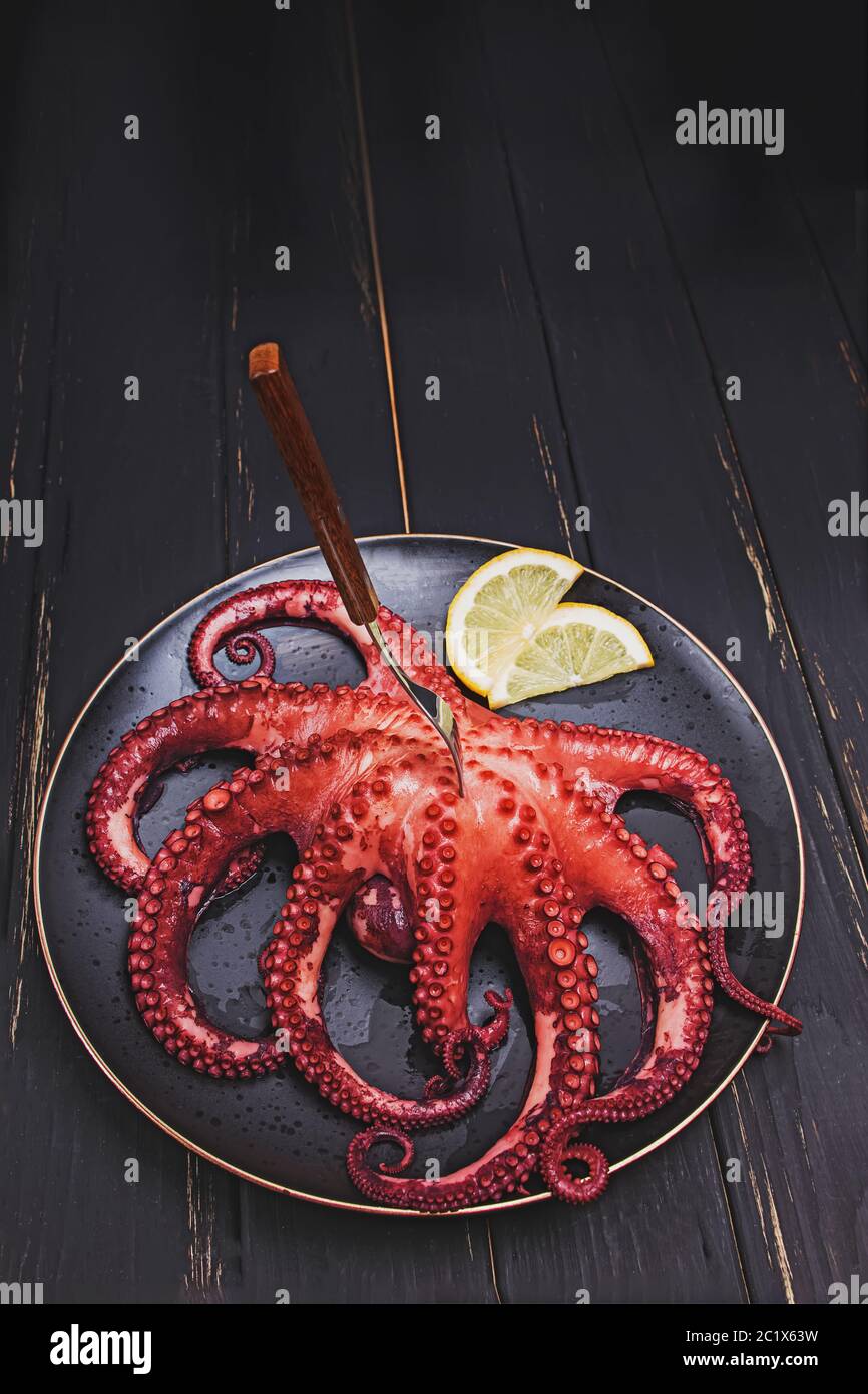 Freshly cooked octopus with fork and lemon on black background ...