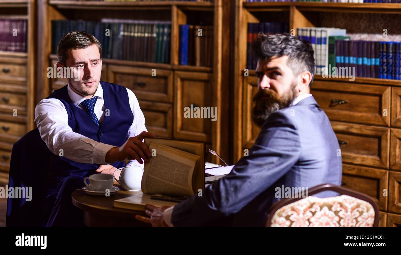 Men in suit with antique bookshelves on background. Professors speaking ...