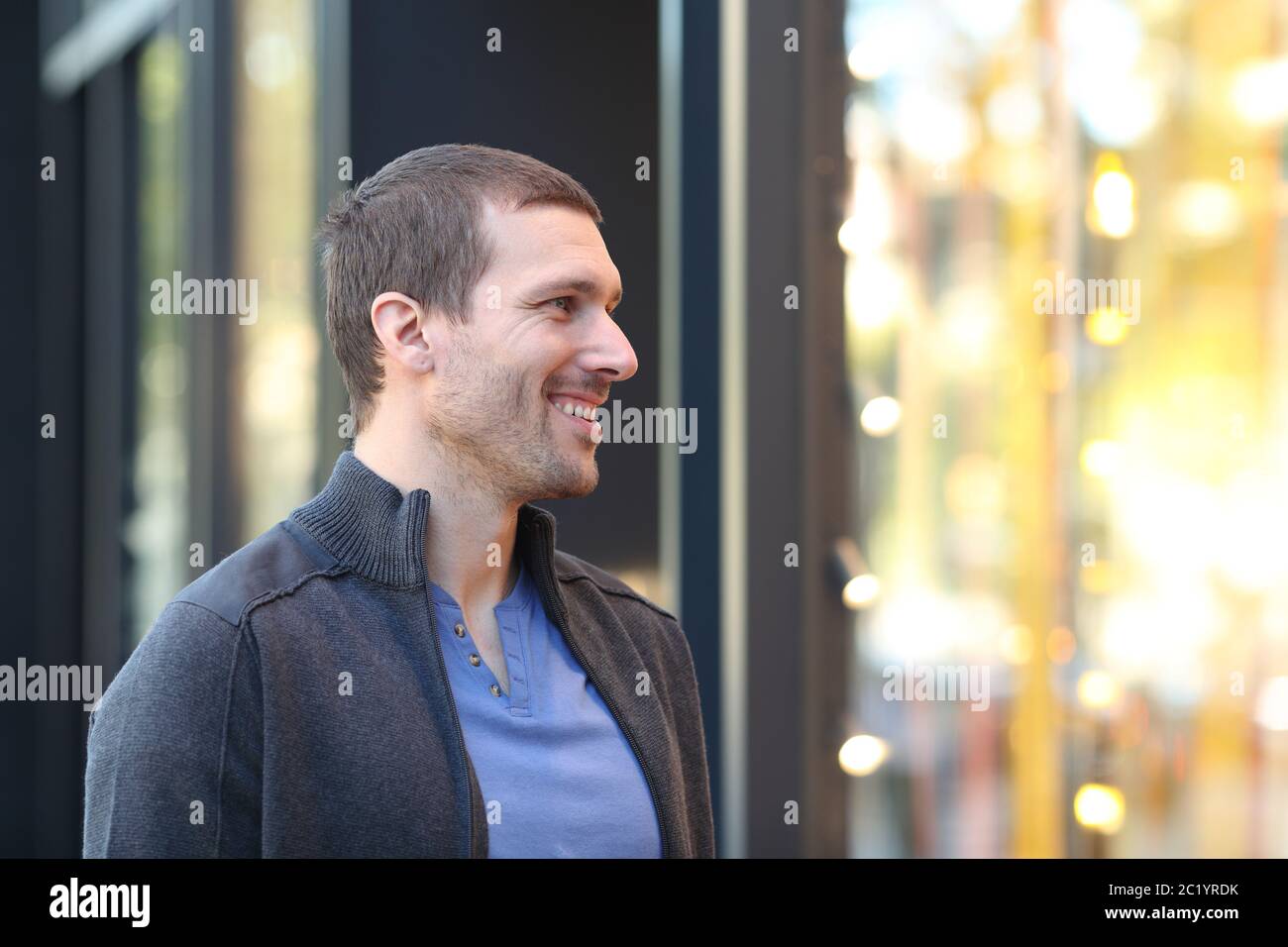 Happy man looking at storefront with lights standing in the street ...